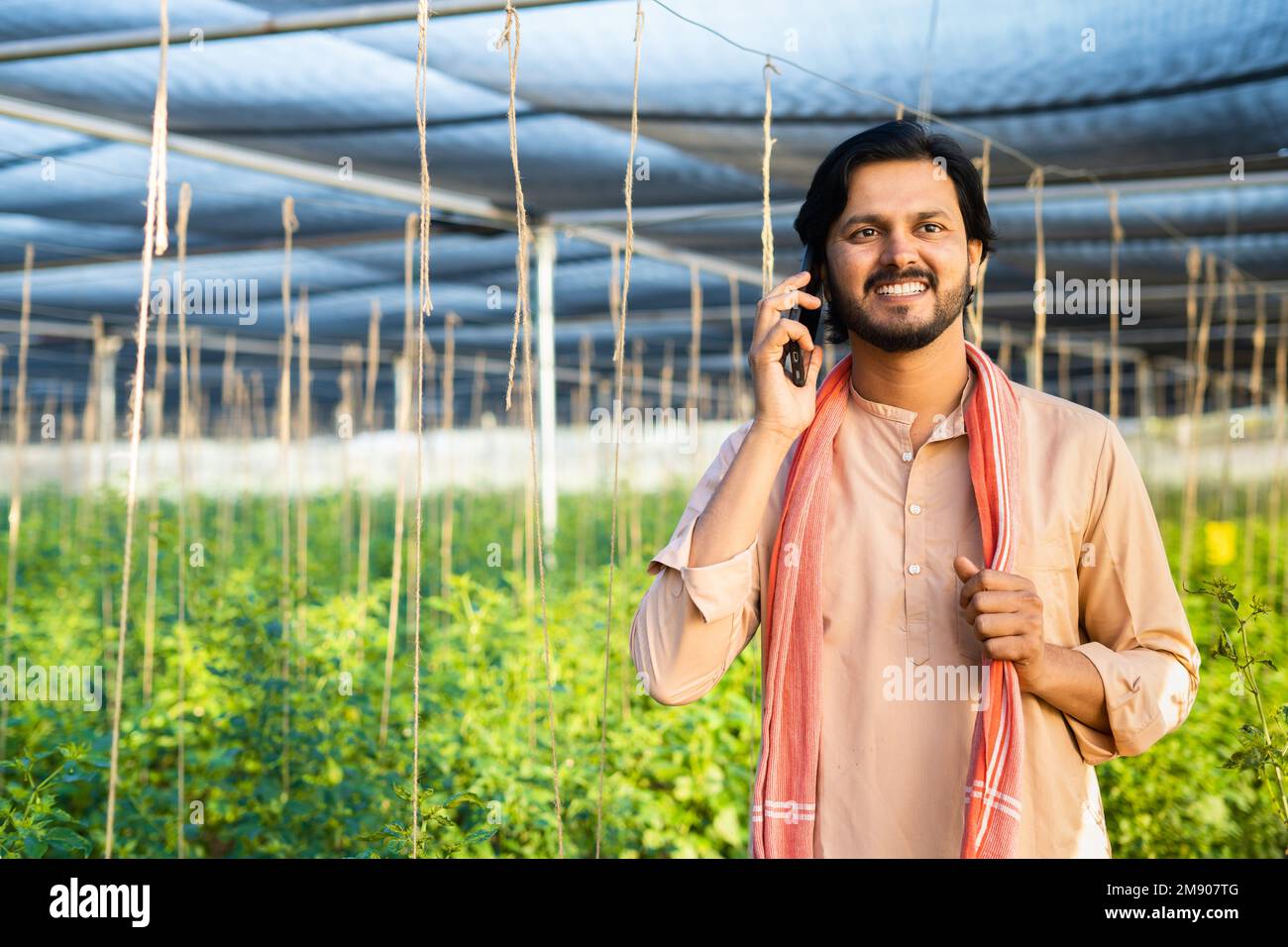Happy smiling young farmer talking on mobile phone at greenhouse ...