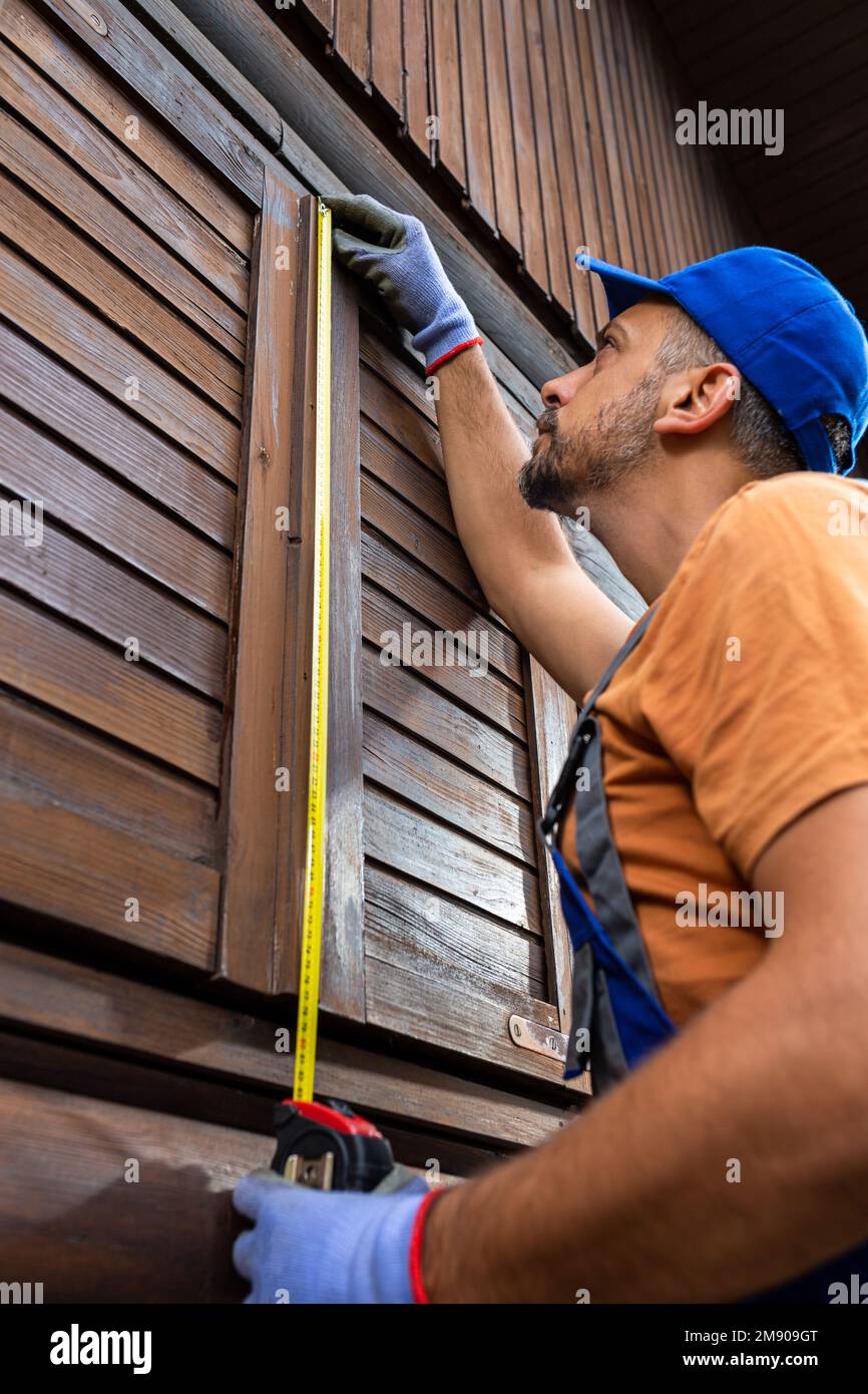 Professional using measure tape for window shutter replacement on ...