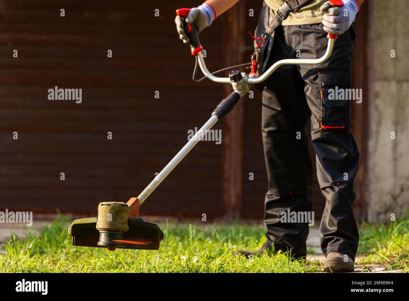 Worker with electric mower in his hands, mowing grass in front of the ...