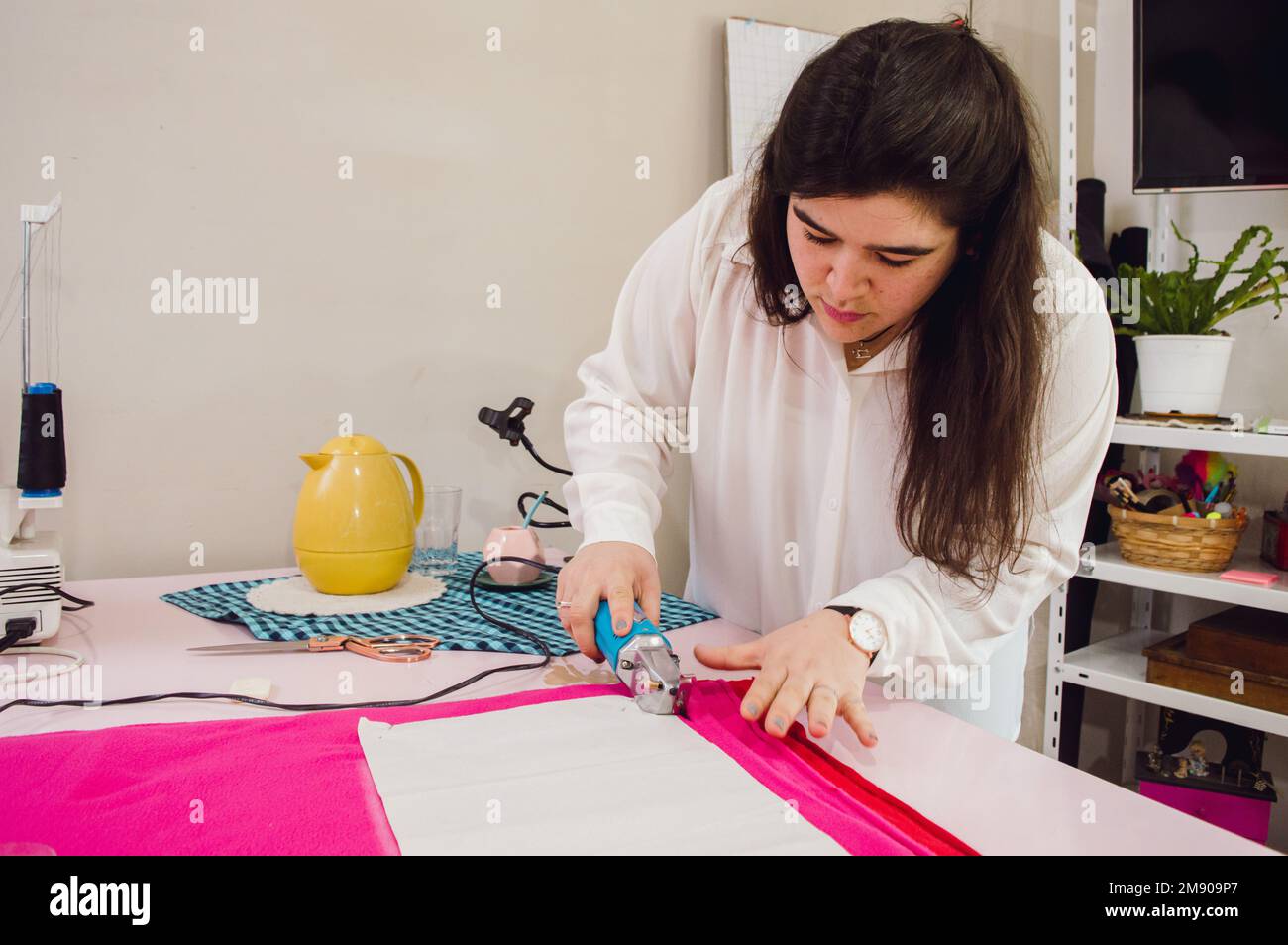 Caucasian young woman with long hair, working with the fabric cutter ...