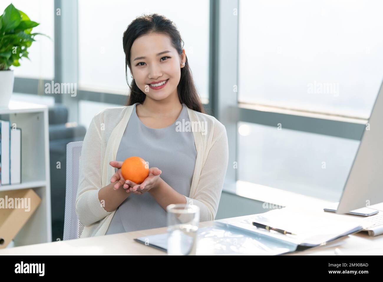 A young woman with an orange in the office Stock Photo - Alamy