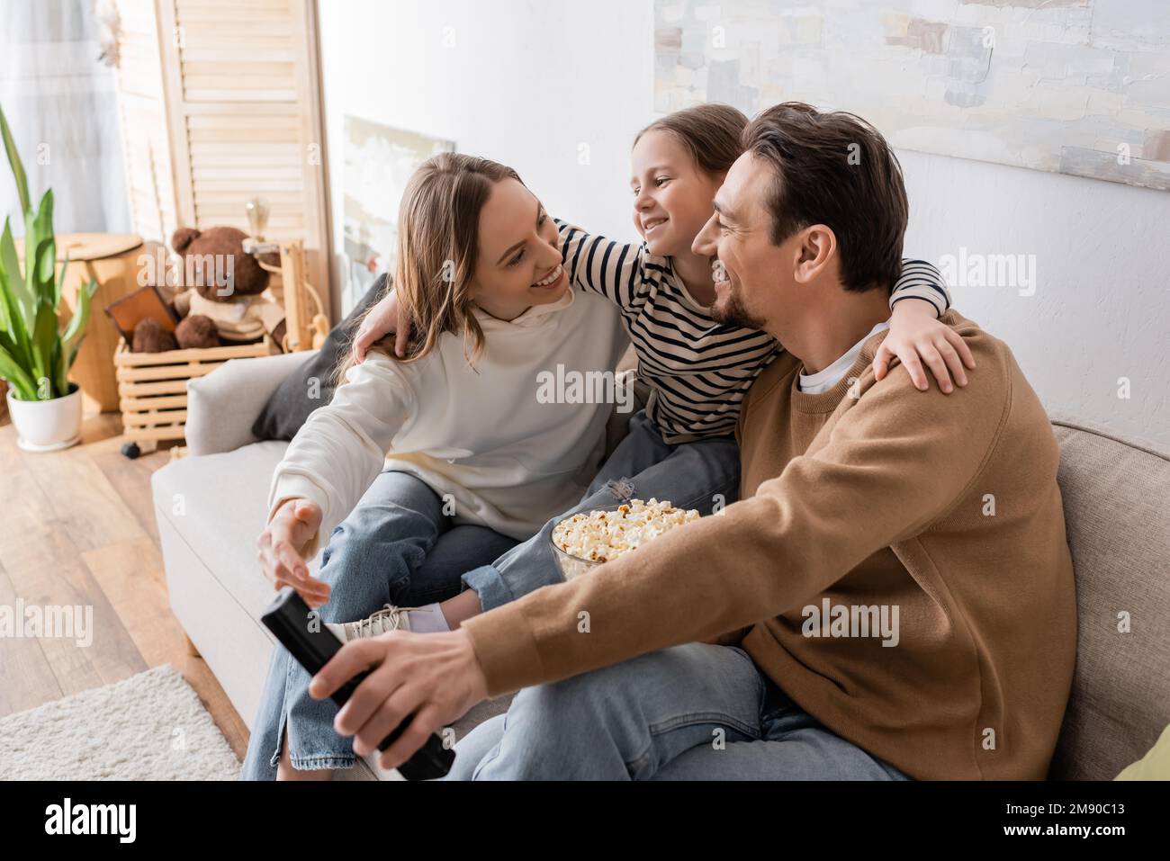 cheerful child hugging happy parents with popcorn and remote controller ...
