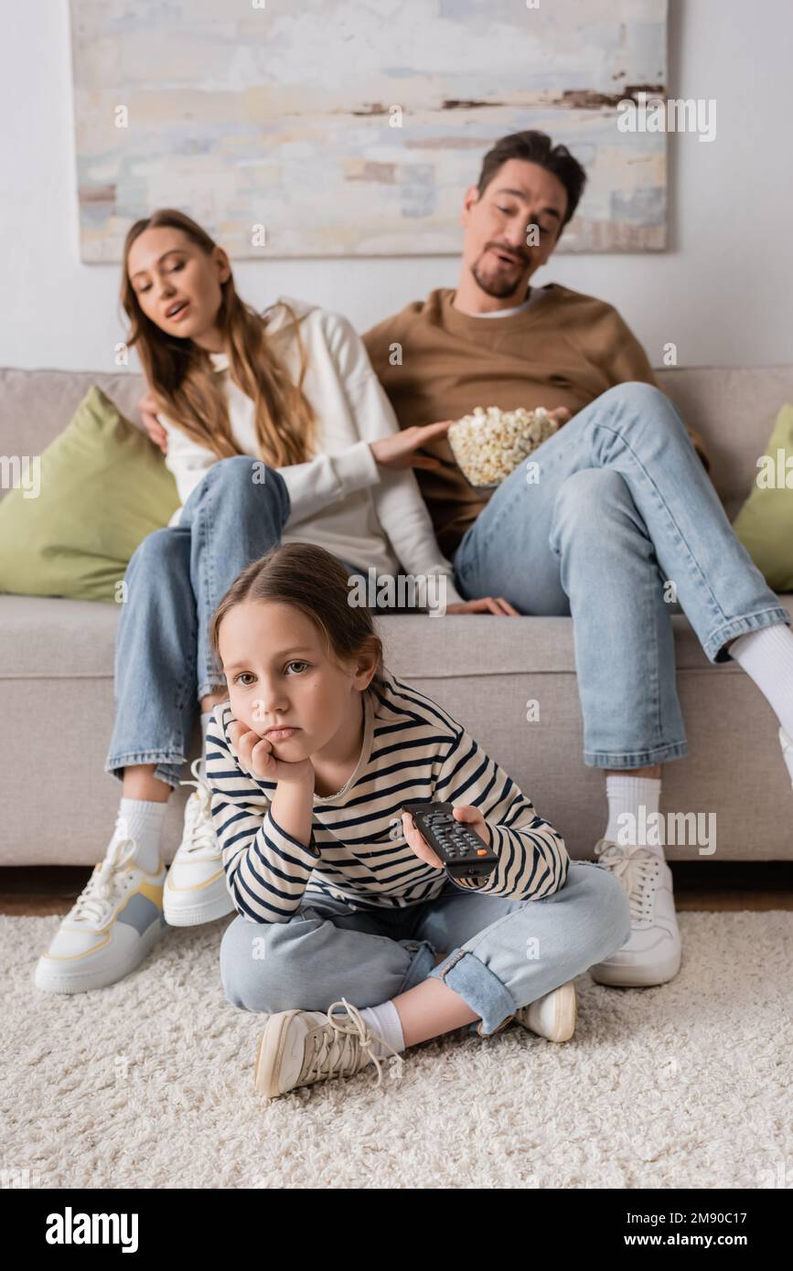 full length of bored kid clicking channels near parents sitting with ...