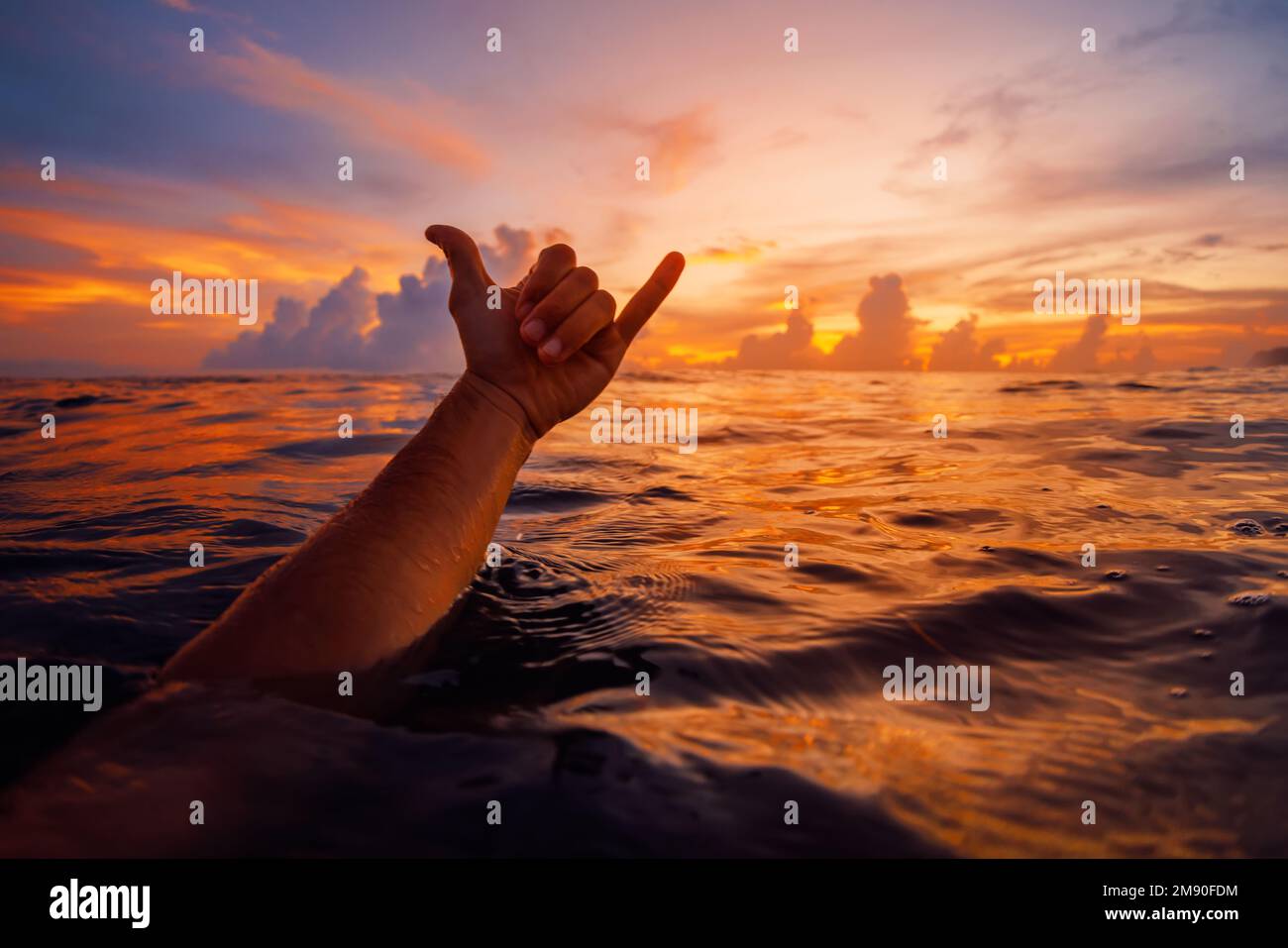 Hand with shaka symbol with colorful sunset in ocean. Lifestyle surfing ...