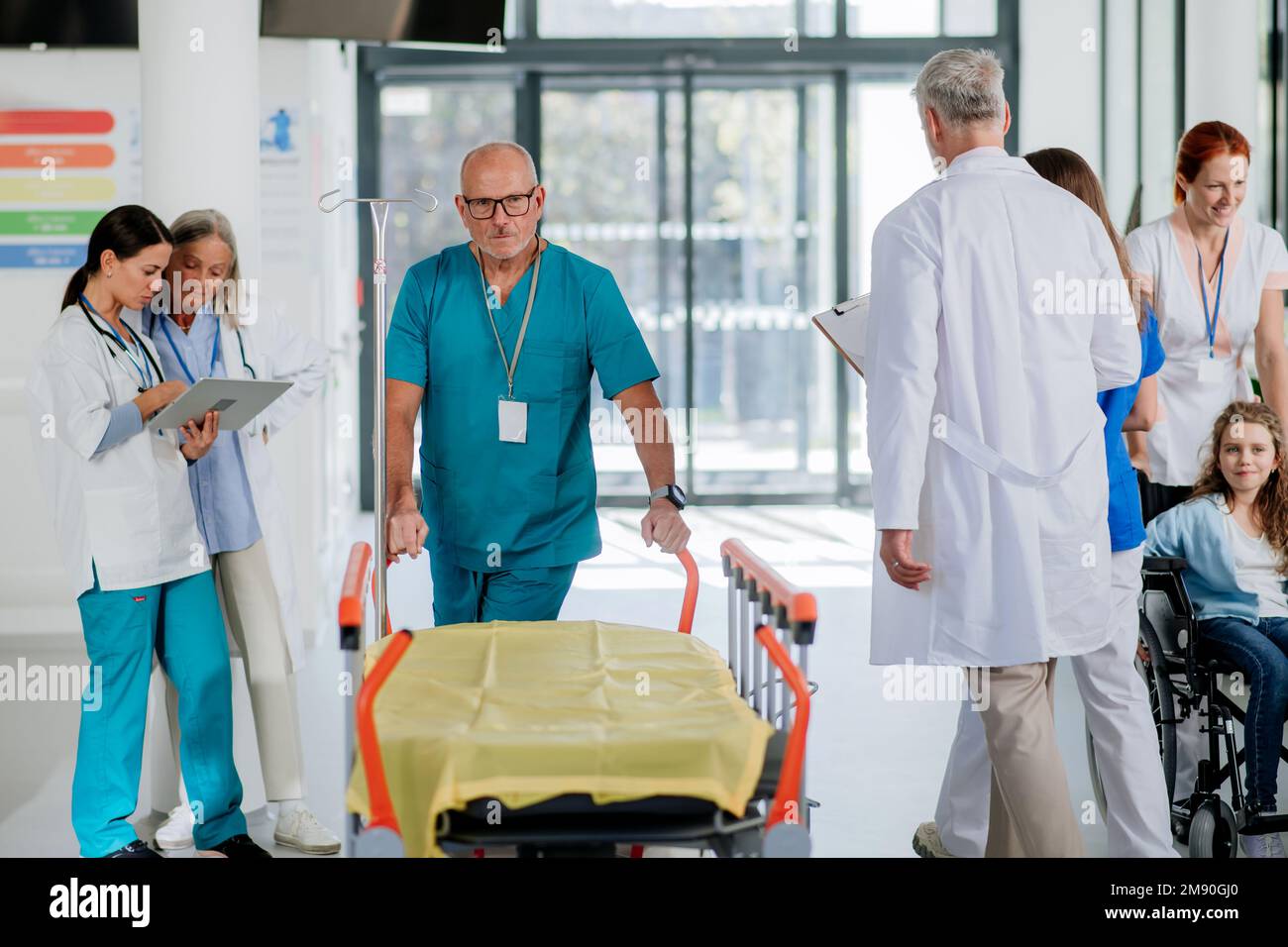 Caregiver pushing hospital bed at corridor, his colleagues taking care ...