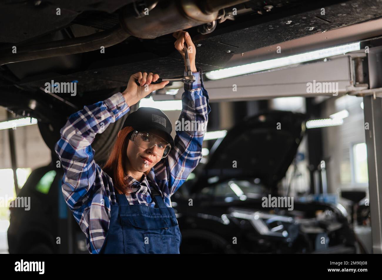 Female mechanic unscrew the nuts on the bottom of the car that is on ...