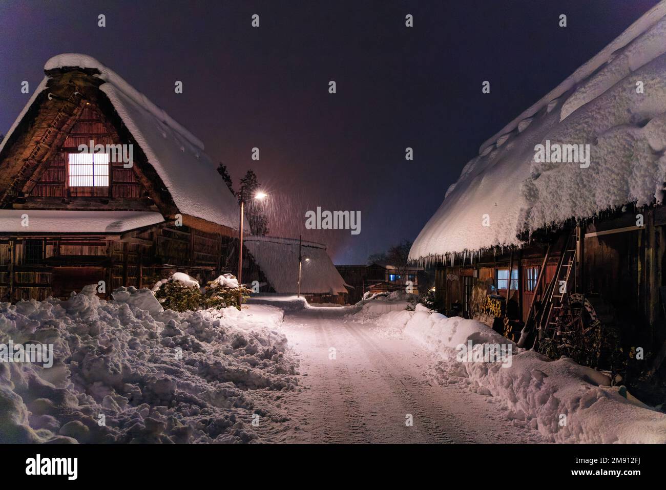 Snow piles along cleared road by traditional wooden houses in village ...