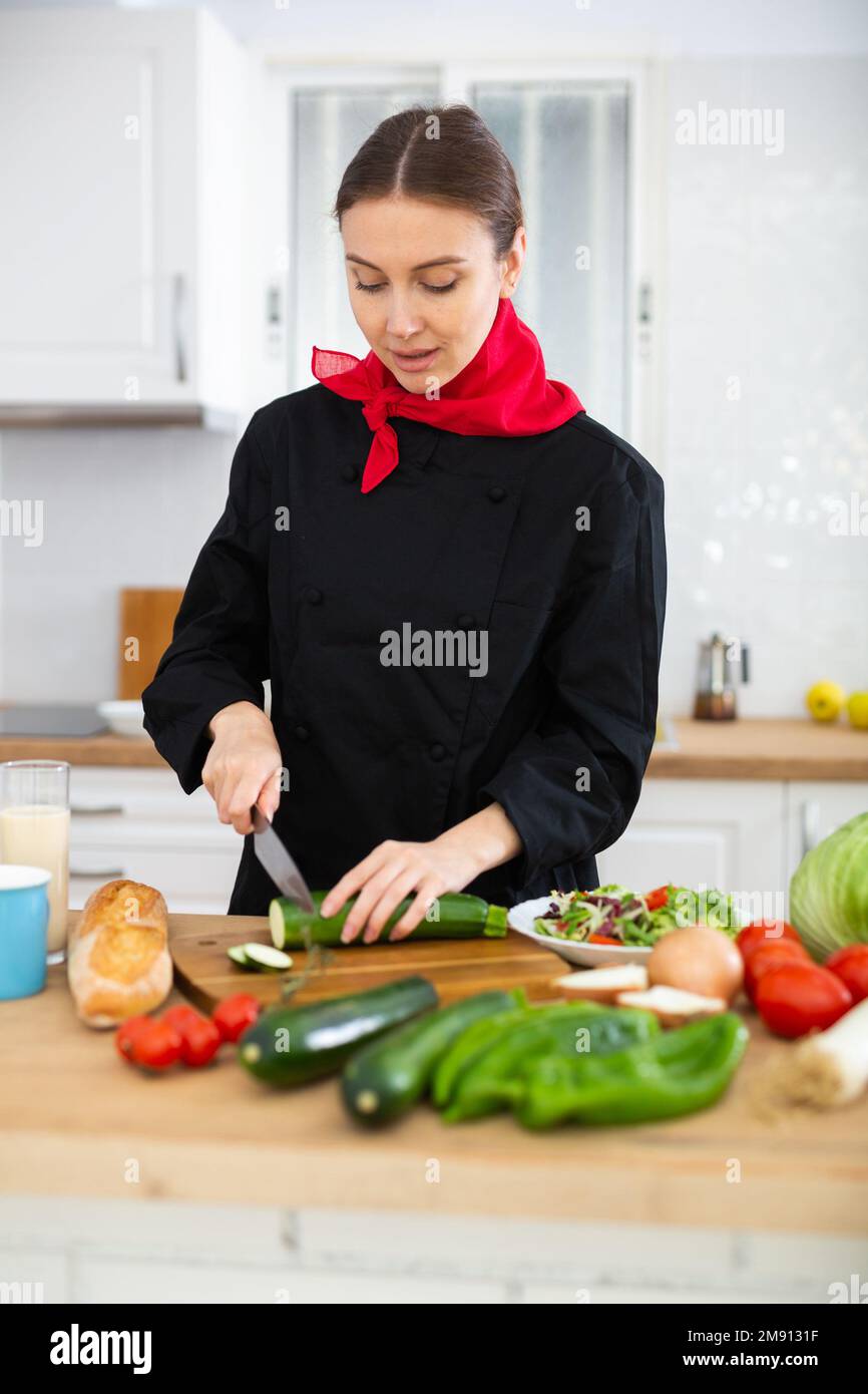 Smiling female chef in black uniform preparing vegetable salad in ...