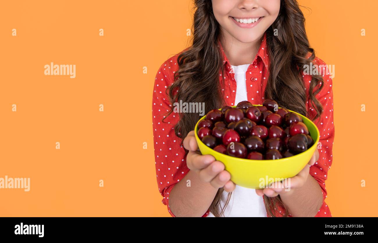 cropped view of kid hold cherry bowl on yellow background. copy space ...
