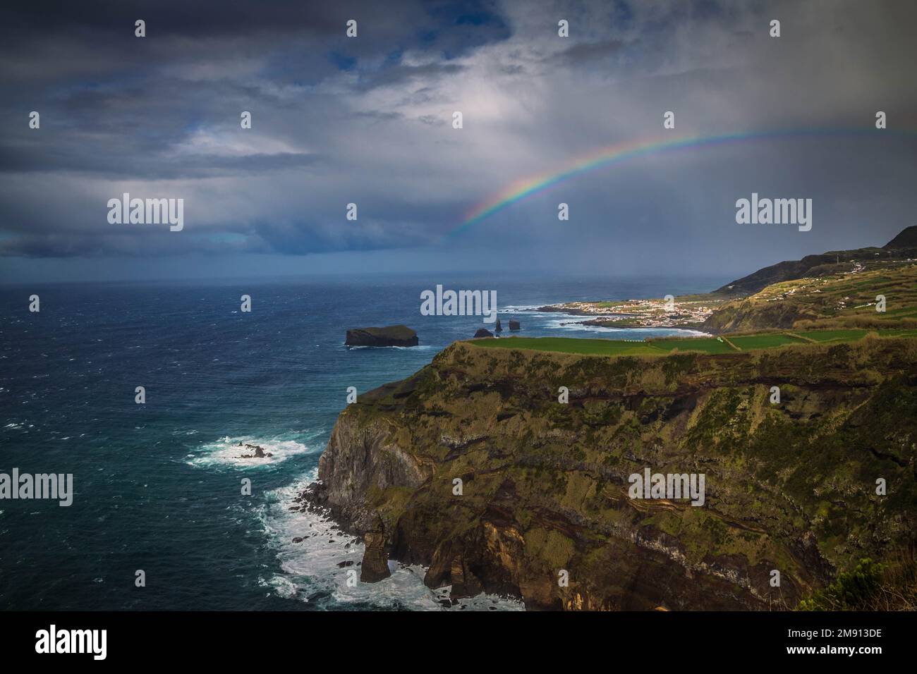 A seascape view with rocky cliffs after rain, a rainbow on a cloudy sky ...