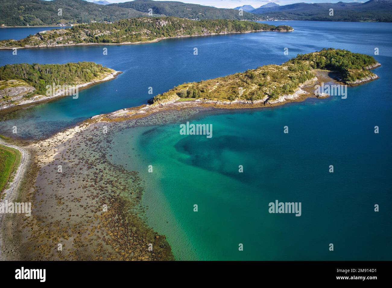 An aerial of a peninsula covered in green trees surrounded by the sea ...