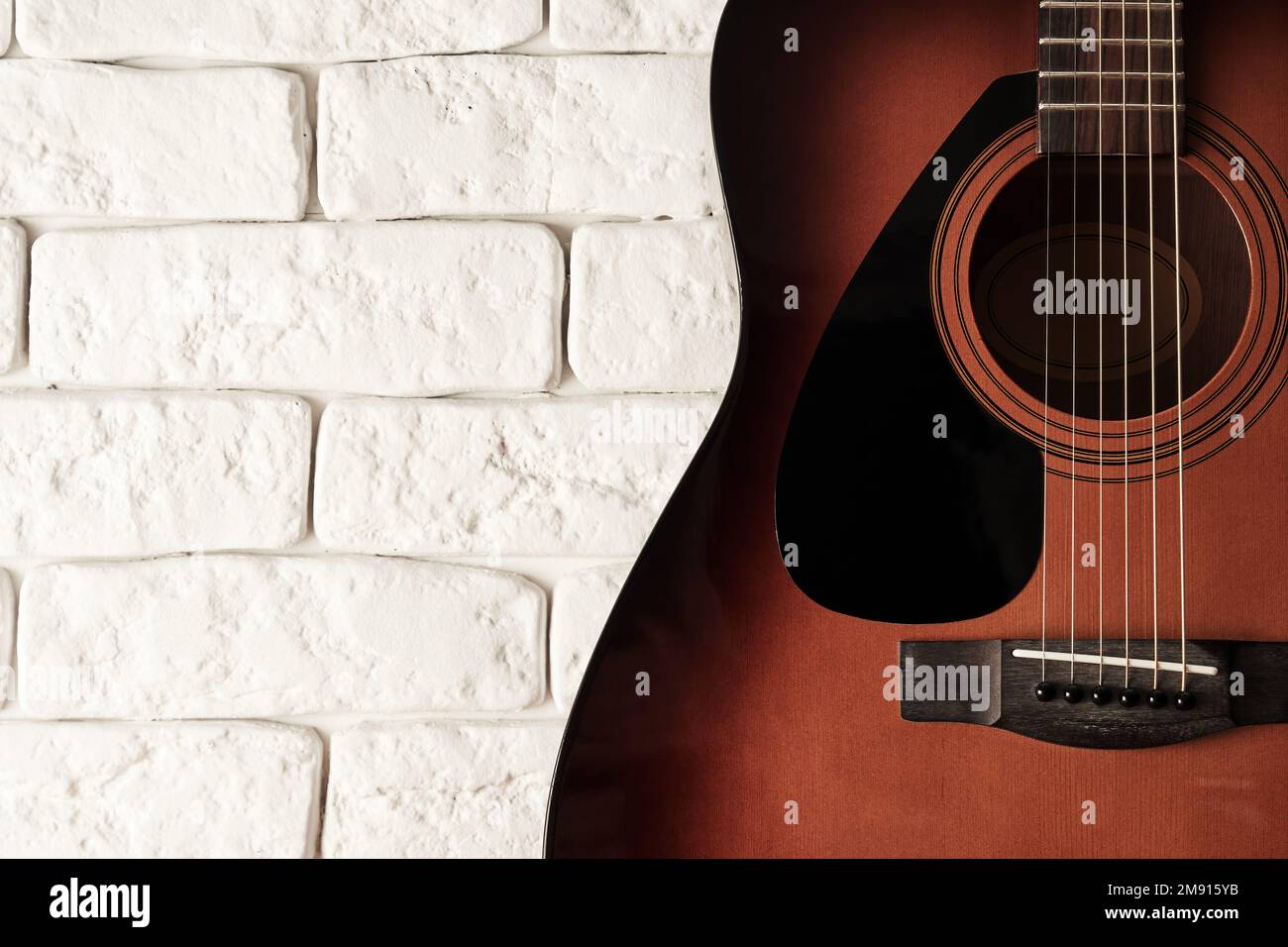 Closeup toned view of acoustic guitar with a white bricks background ...