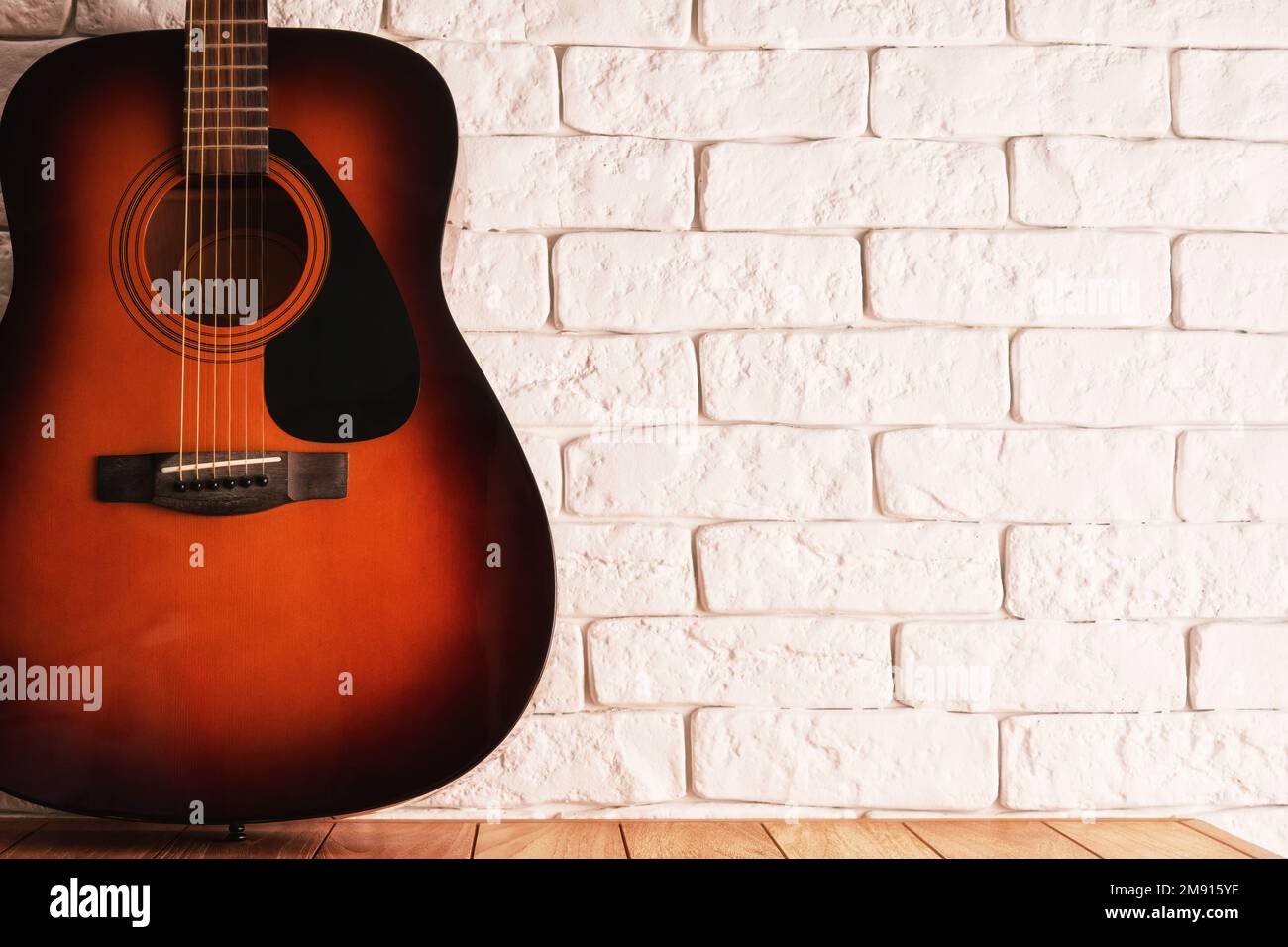 Wooden table with an acoustic guitar and white bricks background ...