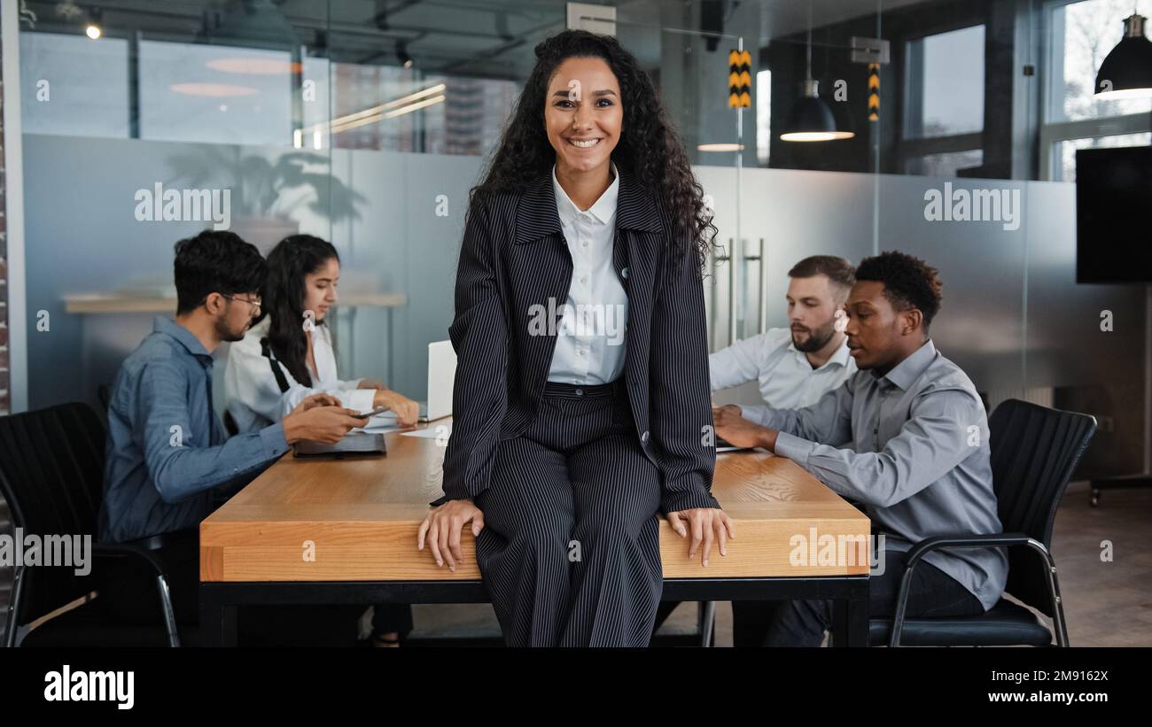 Satisfied smiling female leader boss woman company CEO businesswoman sitting on table in office ...