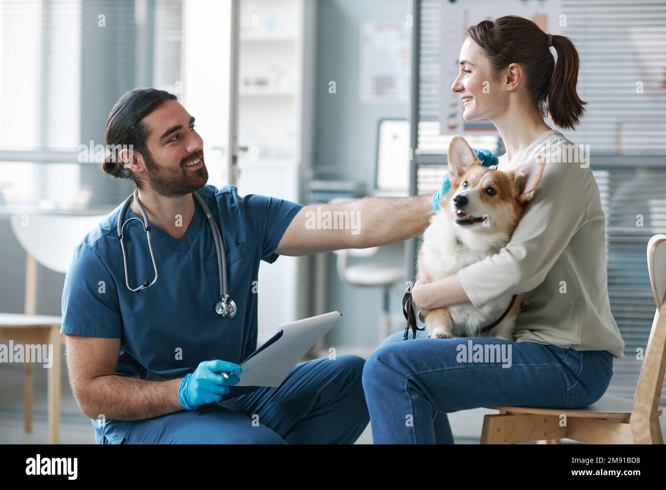 Happy young veterinarian in gloves and uniform consulting female owner ...