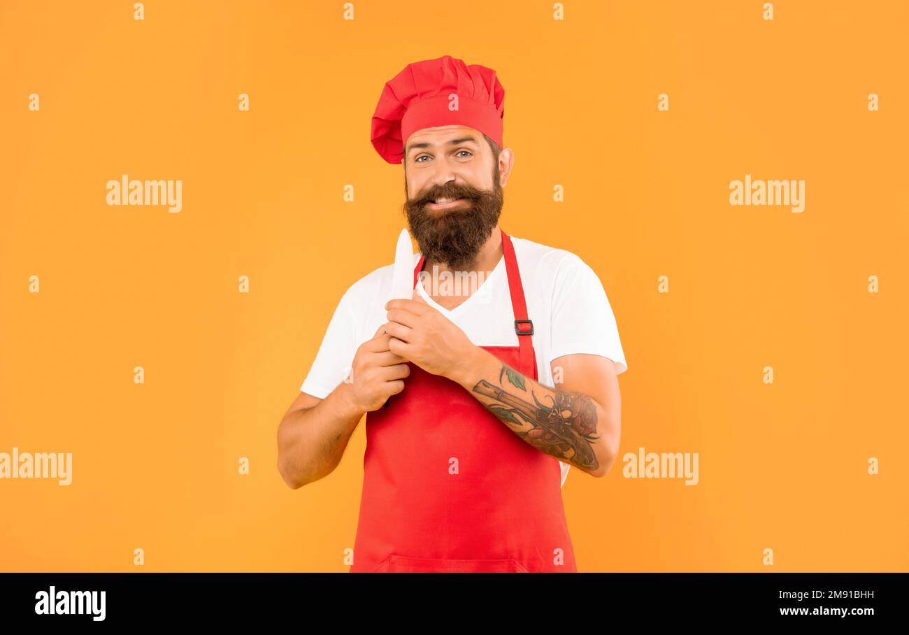 Happy man in red apron and toque holding chefs knife yellow background ...