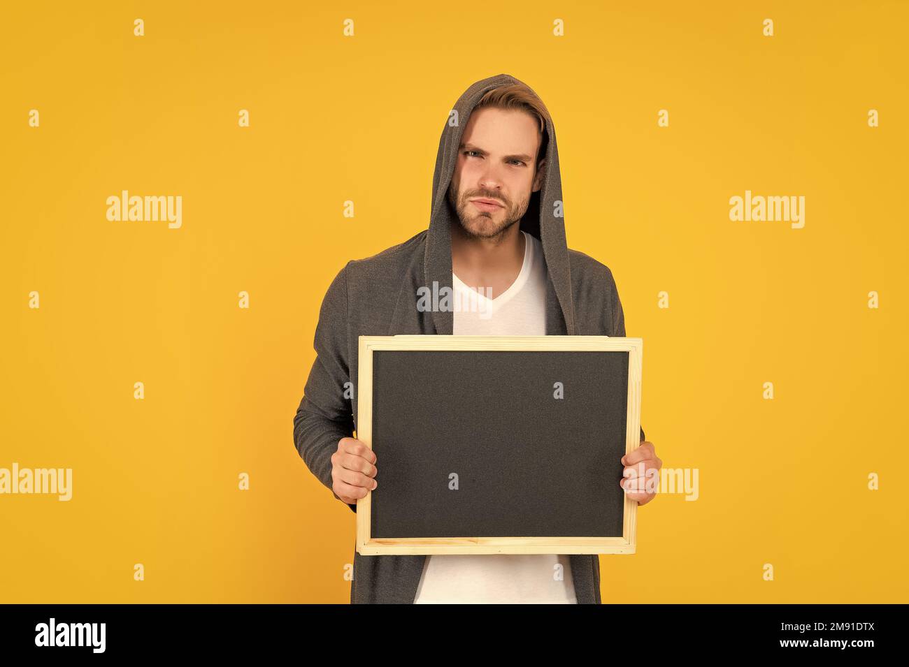 unshaven young man in hood hold blackboard with copy space on yellow ...