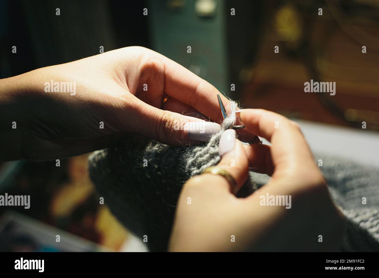 Close up hands knitting the dress from light wool on blurry background. Using circular needles ...