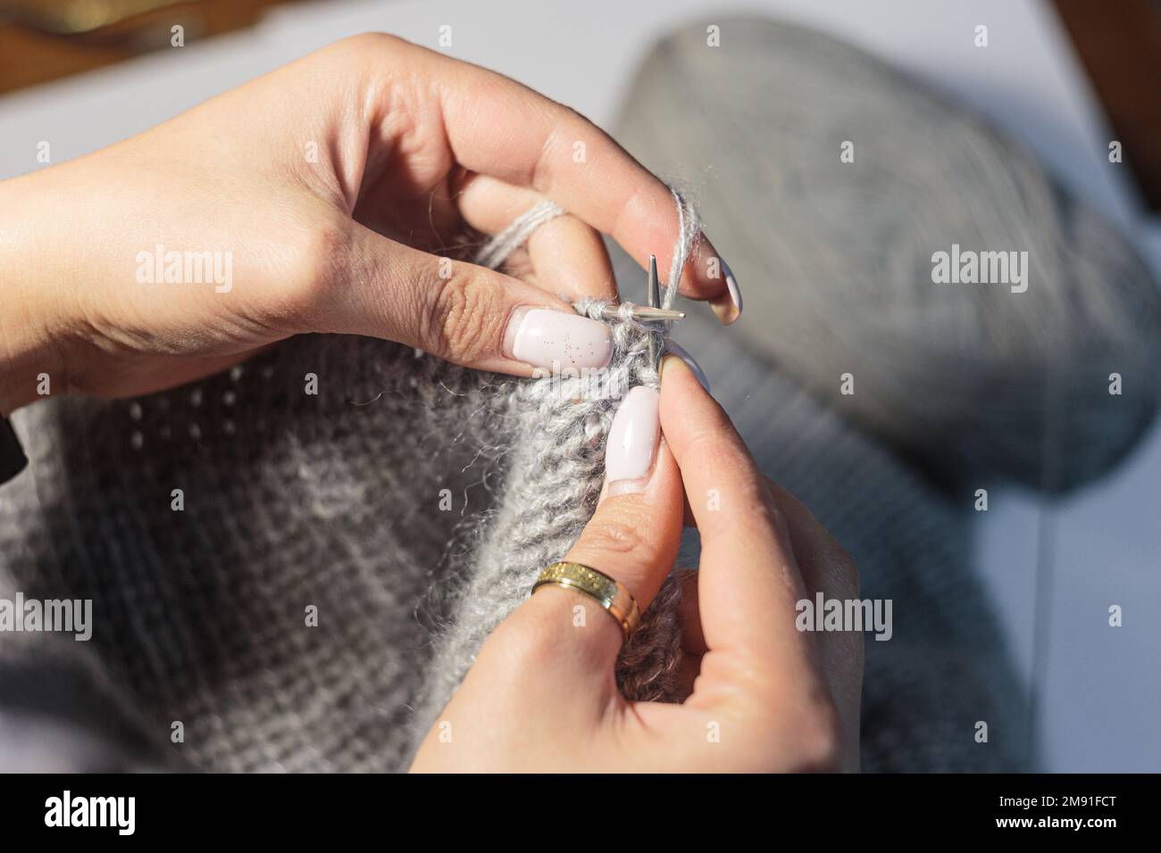 Close up hands knitting the dress from light blue wool on blurry ...