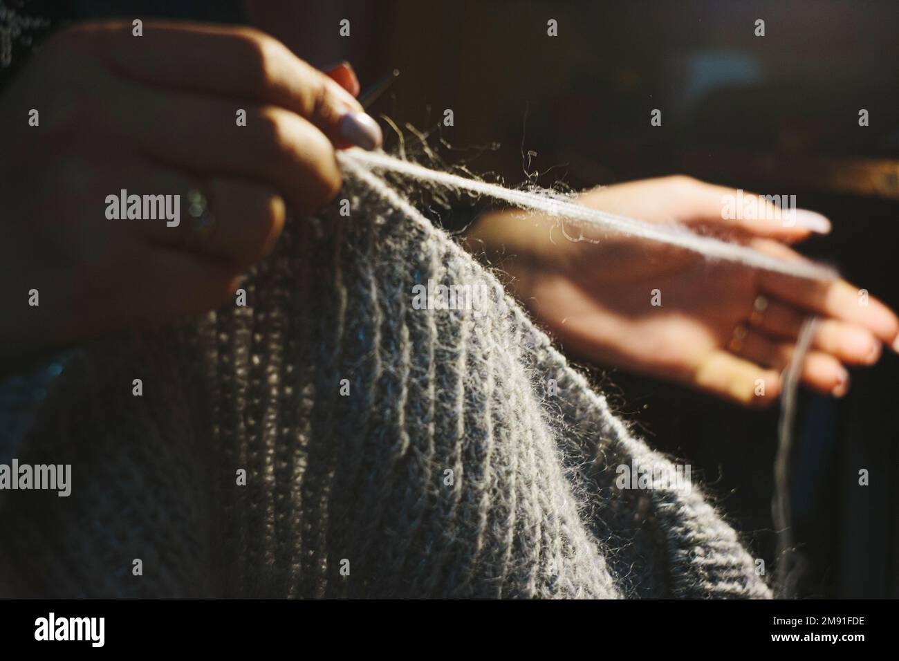 Close up hands knitting the dress from light blue wool on blurry ...
