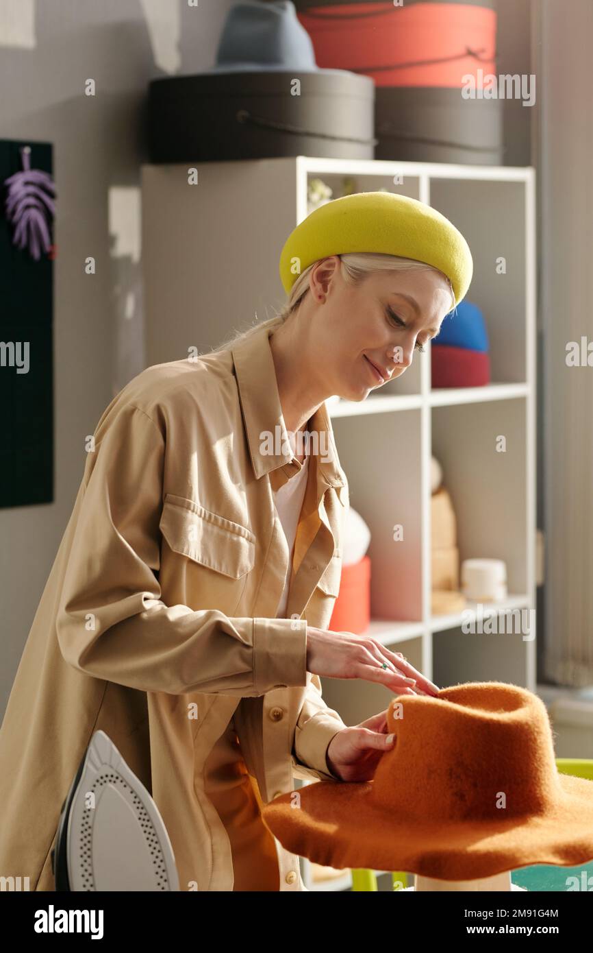 Young craftswoman or hat designer in casualwear and beret fixing shape ...