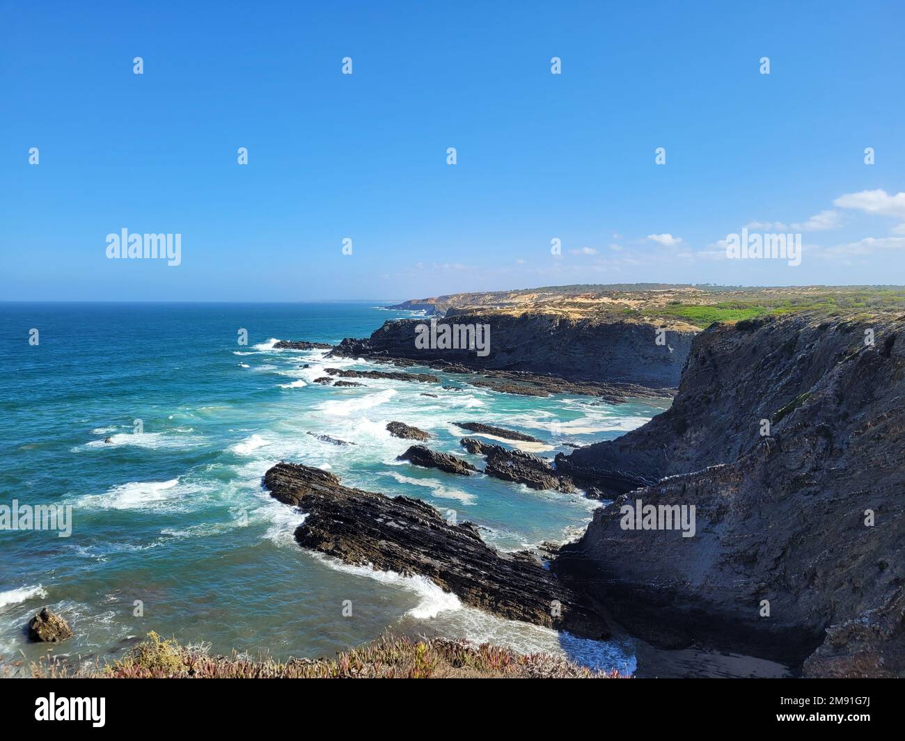 An aerial view of rugged steep cliffs overlooking the sea under blue ...