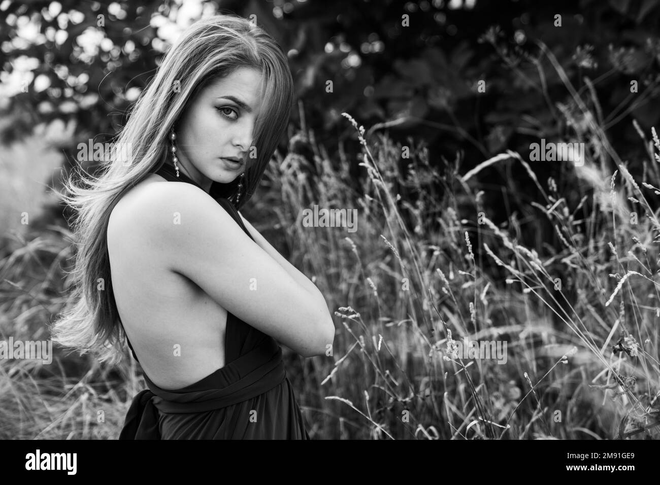 A grayscale shot of a Caucasian woman wearing a dress posing in a wild ...