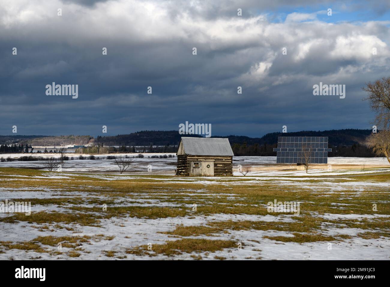 Log cabin shotgun shack with solar panel in farmers field with snow and ...