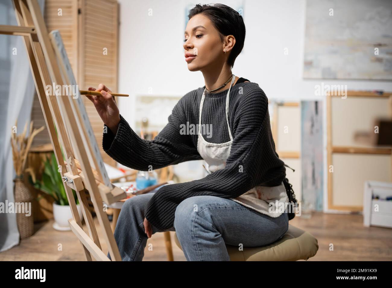 Short haired artist sitting and painting on canvas in studio Stock ...