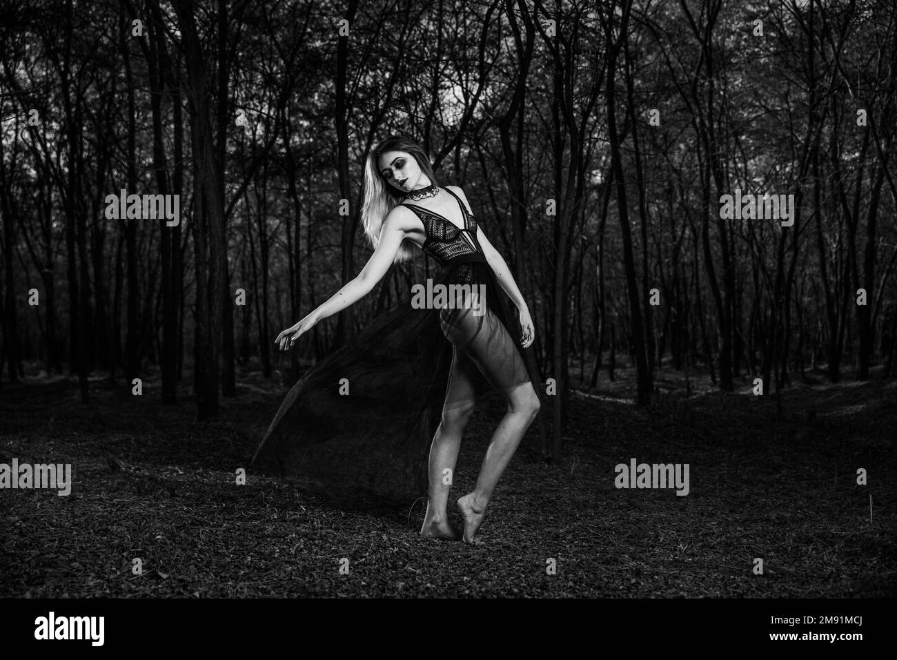 A grayscale of a gothic young girl in black transparent dress posing in ...