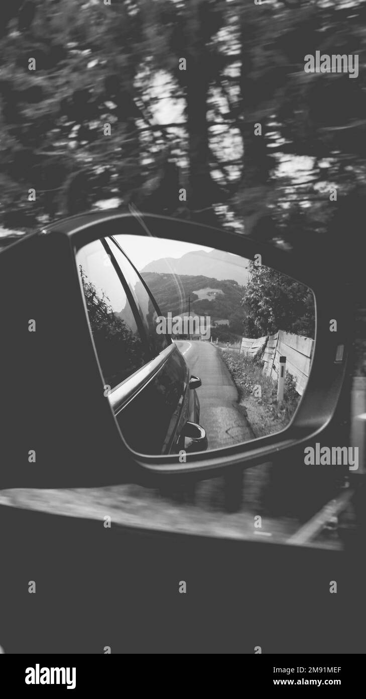 A vertical grayscale of the side mirror of a car with the road ...