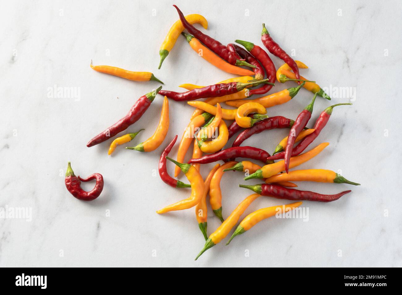 Spicy red and orange thai chilles on a white marble background; harvest ...