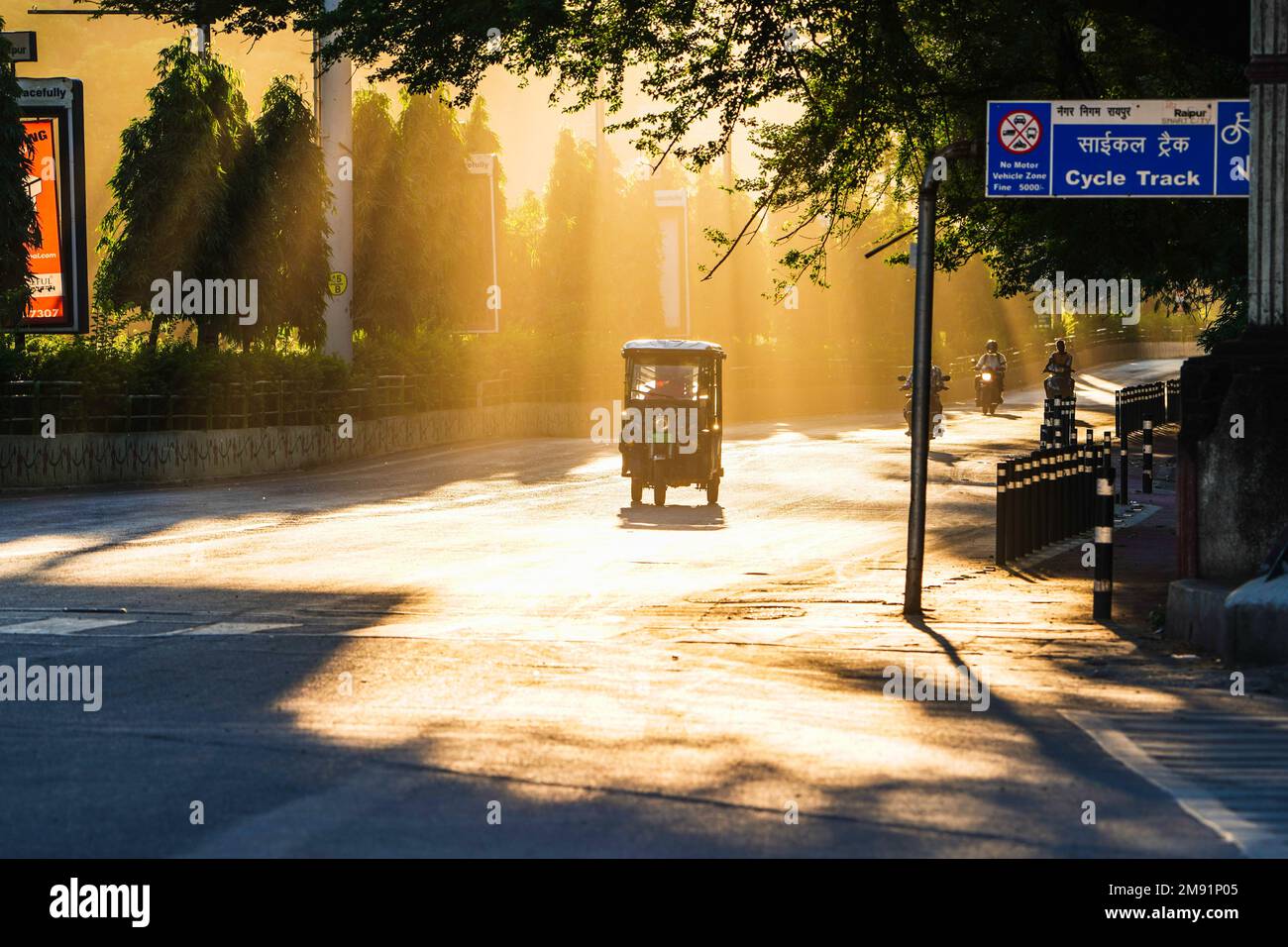Beautiful yellow sun rays touching the empty road of raipur, an electrical auto rishaw passing ...
