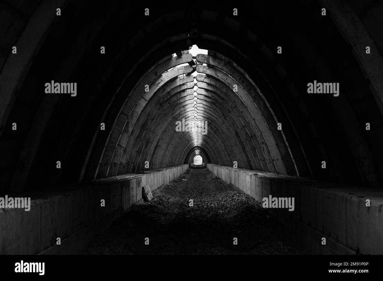 A black and white of a long stone tunnel with ceiling lights in the ...