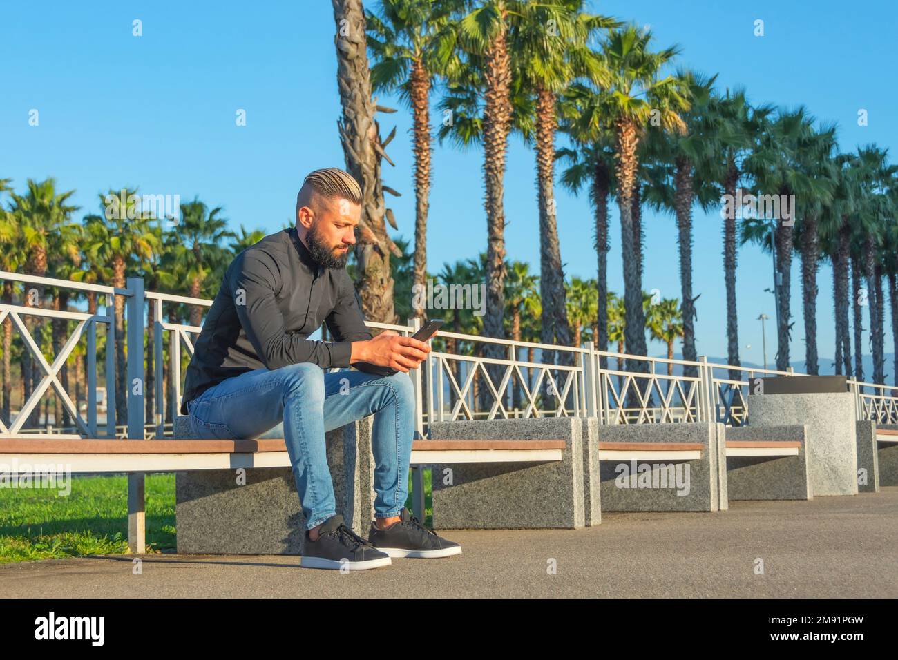 Middle aged man with slicked back hair and beard sits bench near alley ...