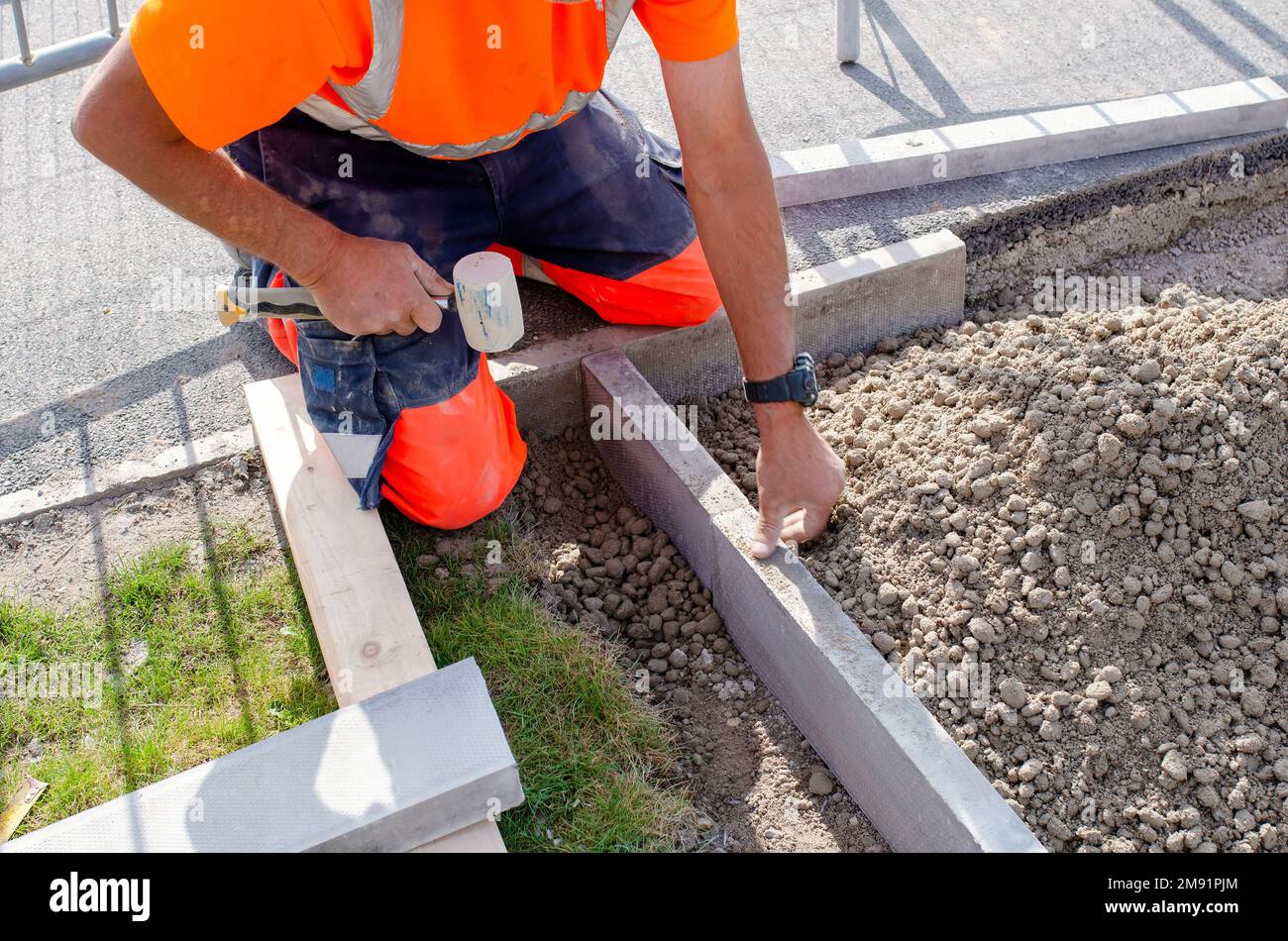 Builder in orange ho-viz protective closing placing edging pin kerb ...