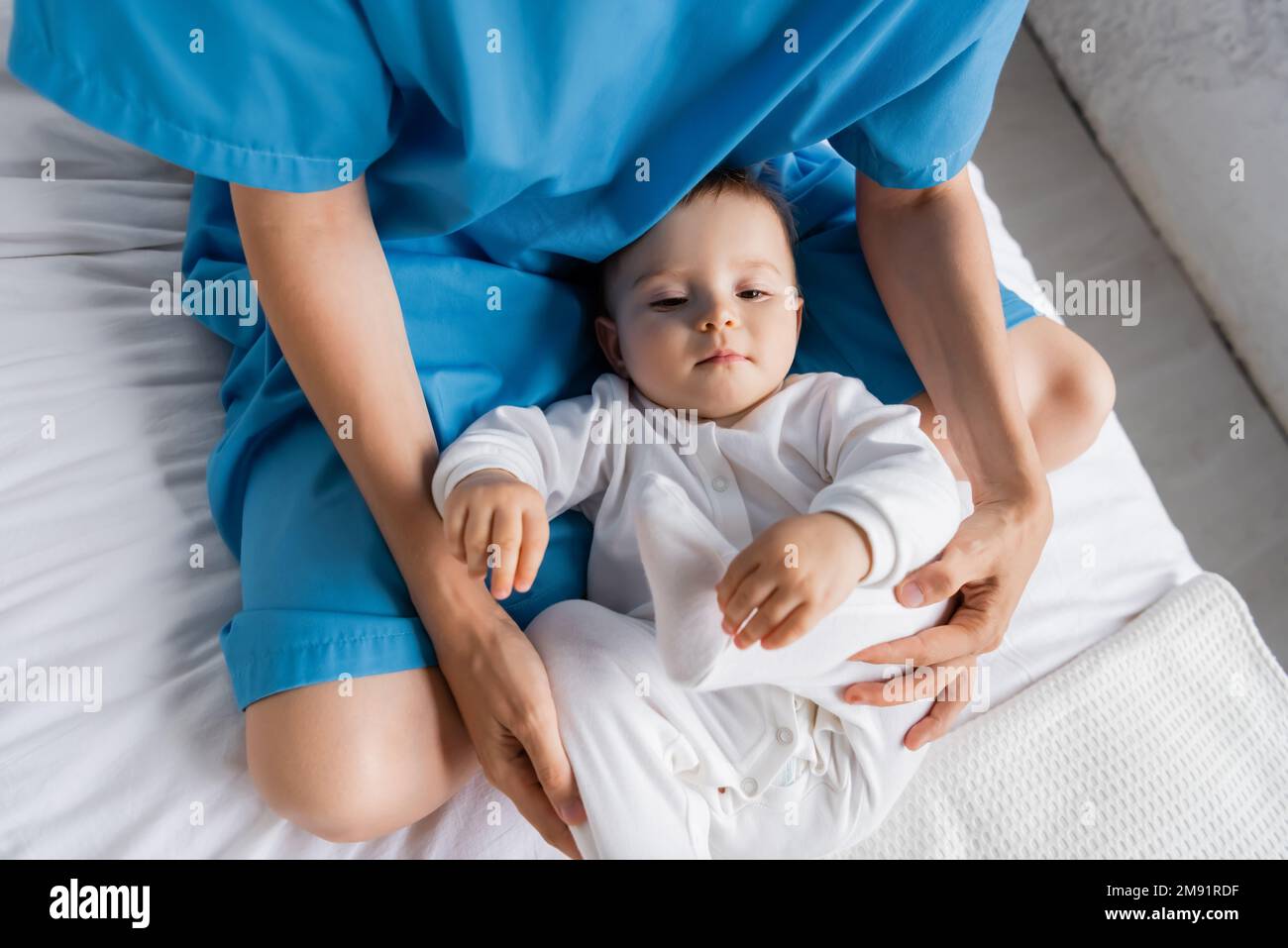 top view of toddler child in romper near mother in patient gown sitting ...
