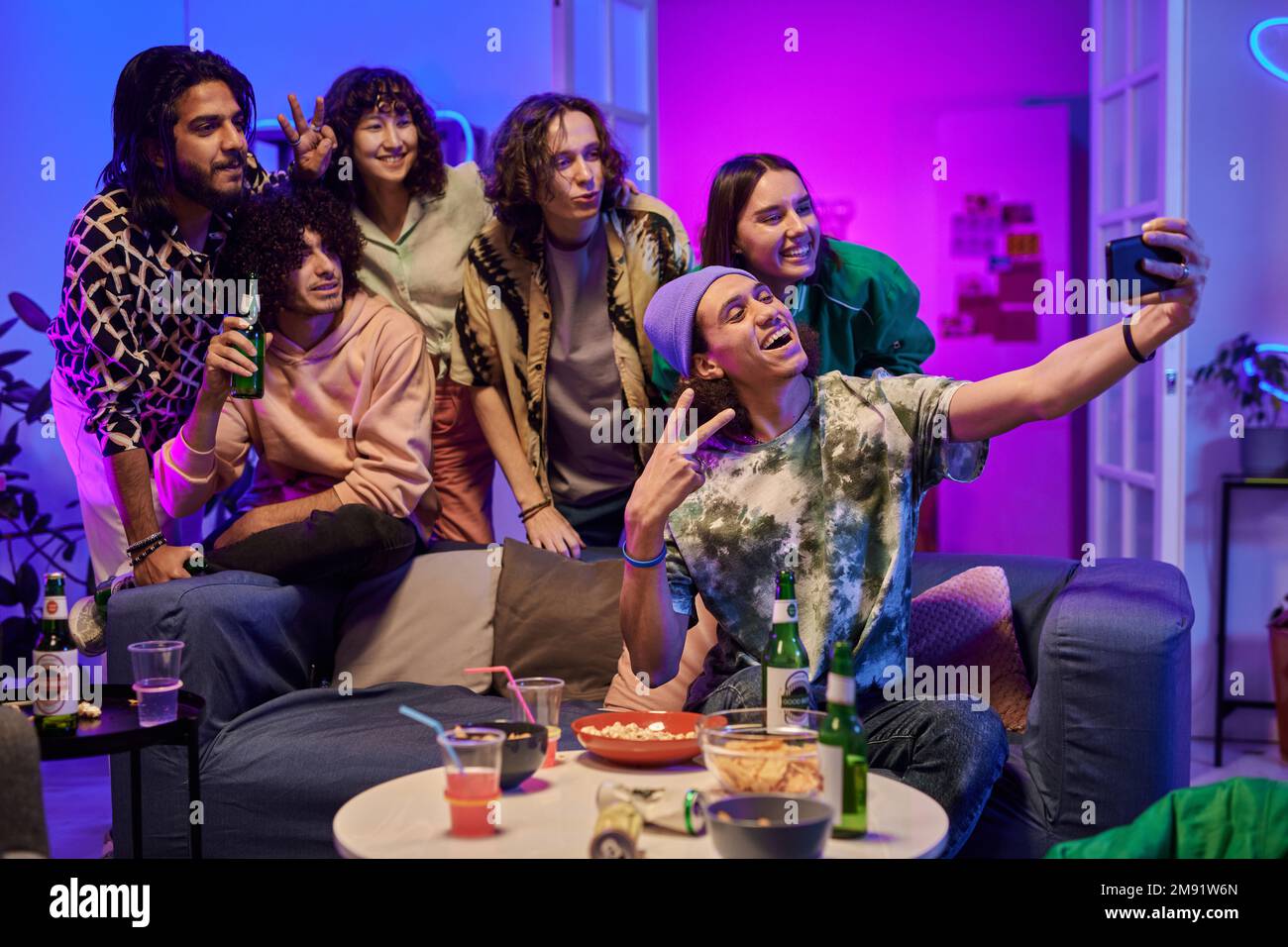 Large group of happy young intercultural friends gathered by couch and ...