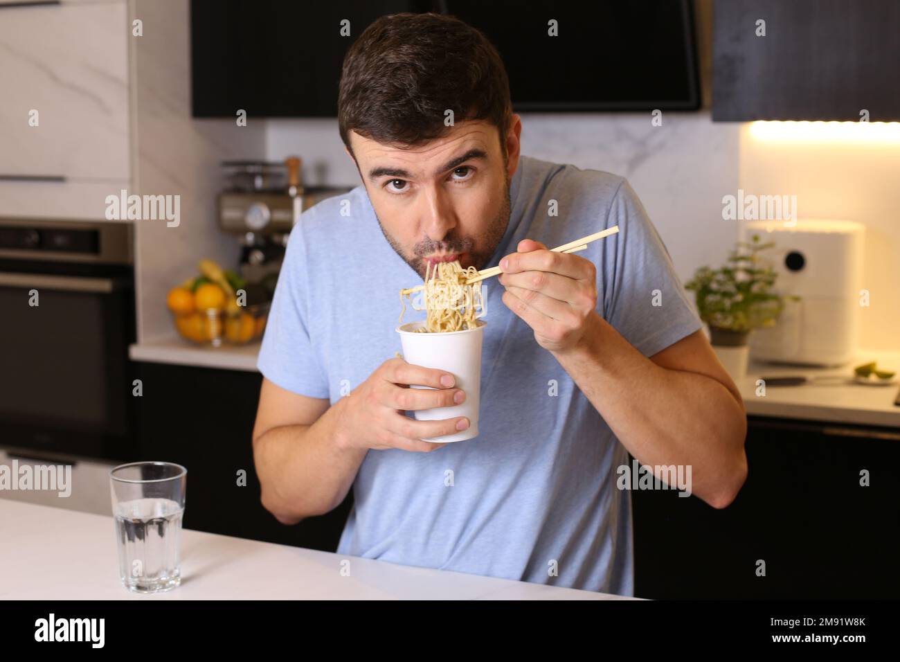 Cute guy eating instant noodles in the kitchen Stock Photo - Alamy