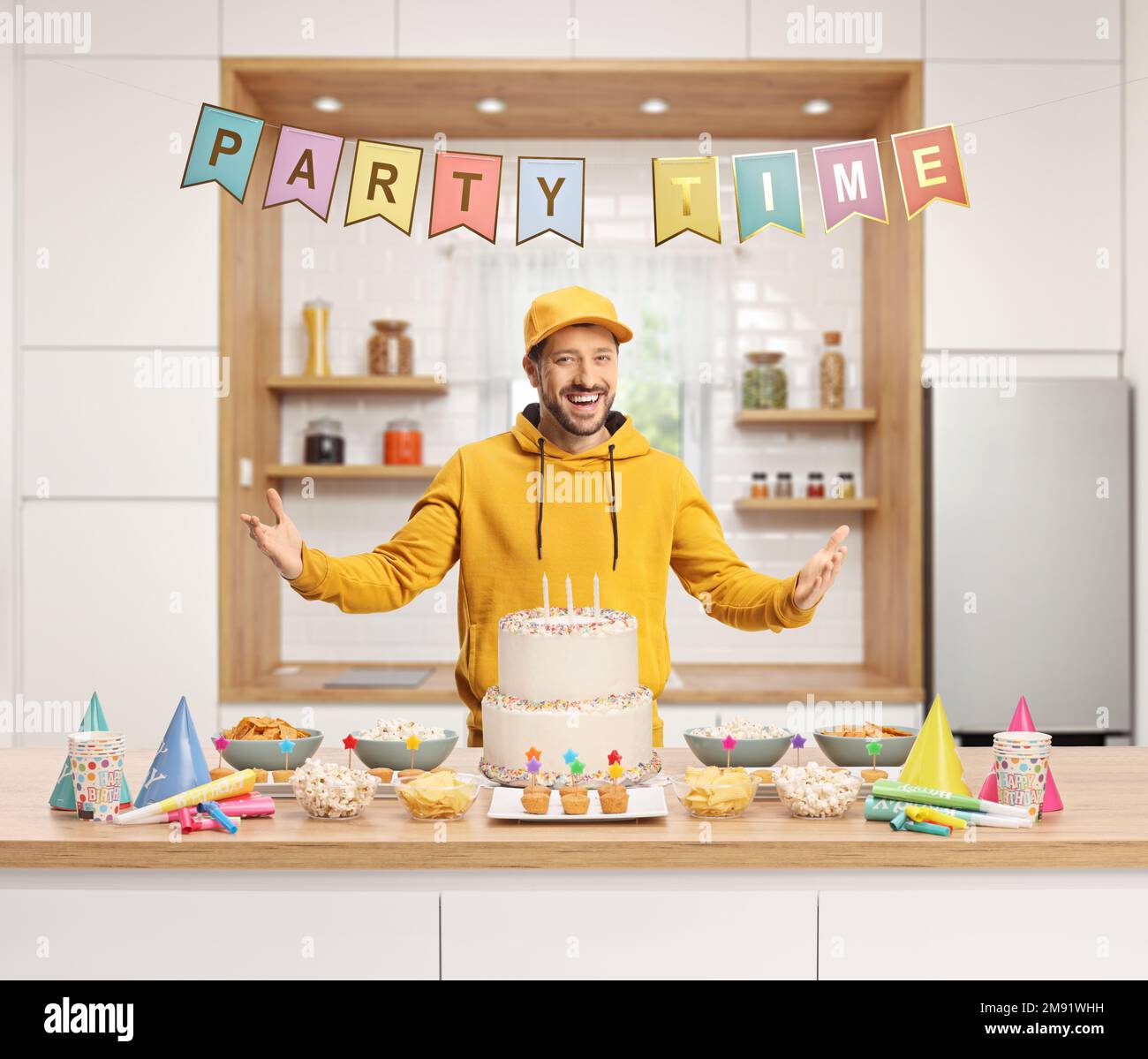 Guy posing behind a counter with party snacks and a cake inside a ...