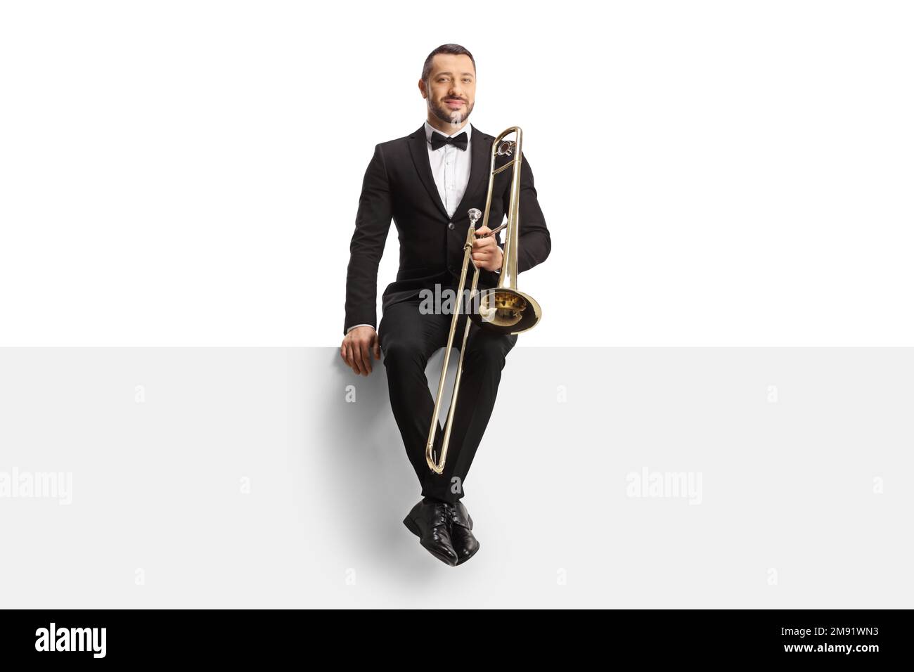 Male musician in a black suit and bow-tie sitting on a blank panel with ...