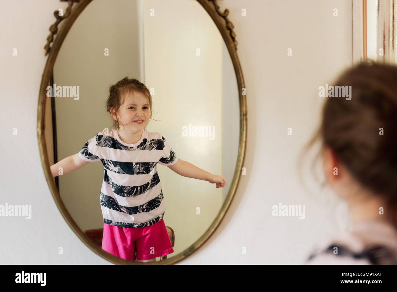 Happy little girl is standing in front of a mirror at home Stock Photo ...