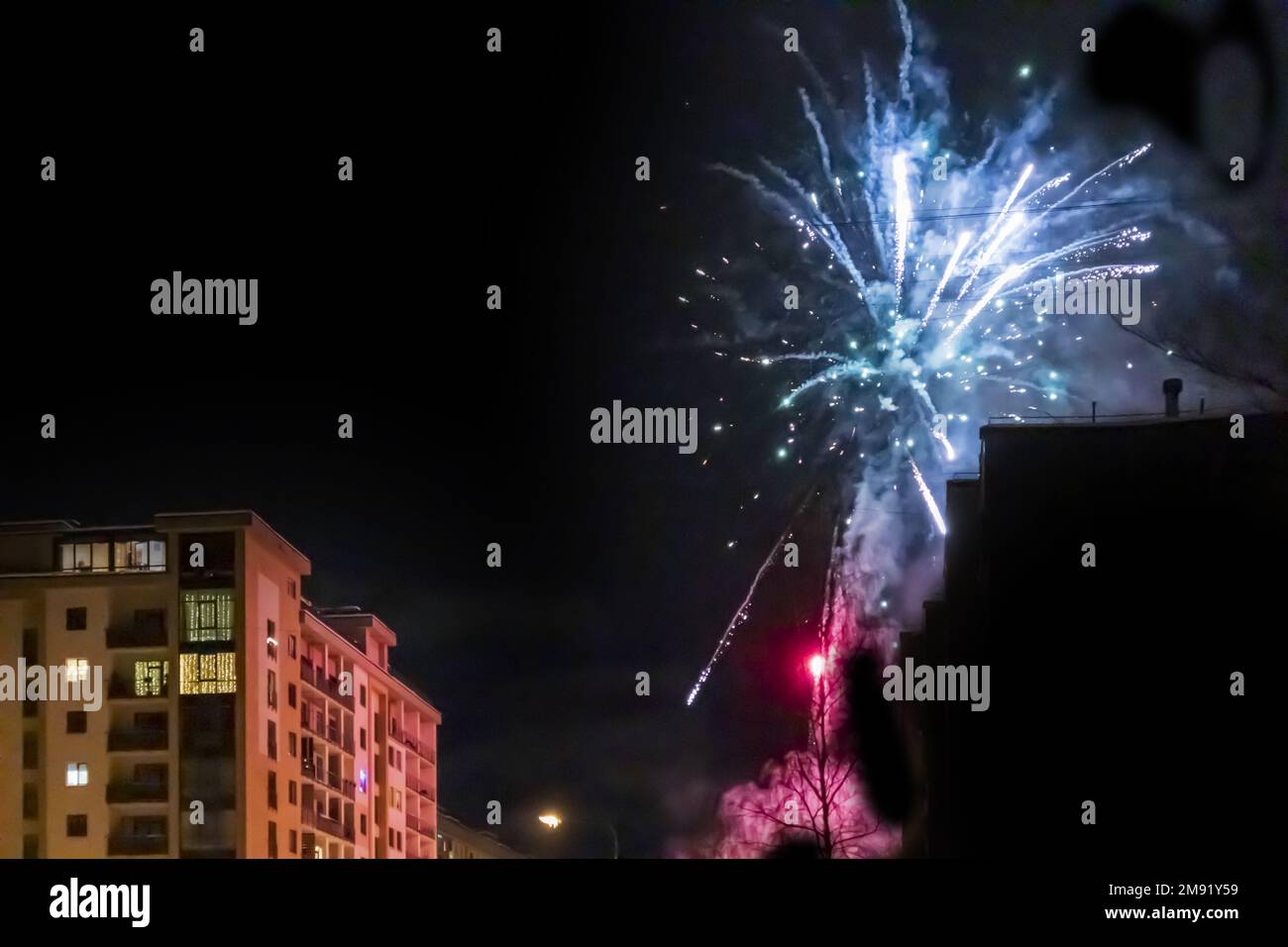 A colorful rocket firework in front of a city house against a dark sky ...