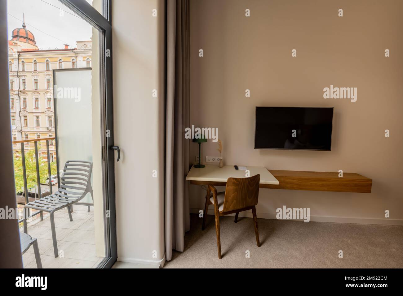 flat tv screen on wall near workspace with chair and balcony in hotel ...