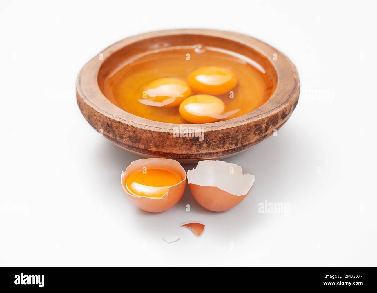 Three egg yolks in wooden plate on white table background with shell ...