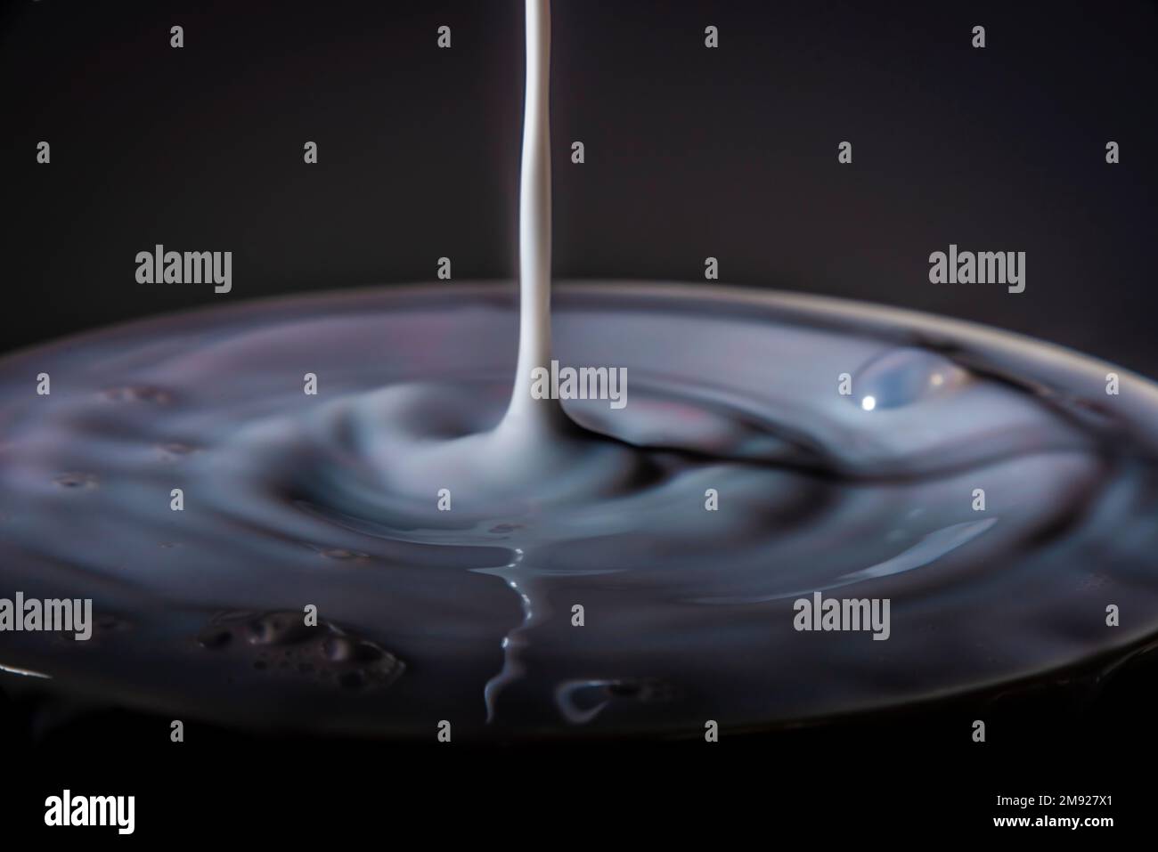 Color fresh sweet milk drops into another color of milk in cup with ...