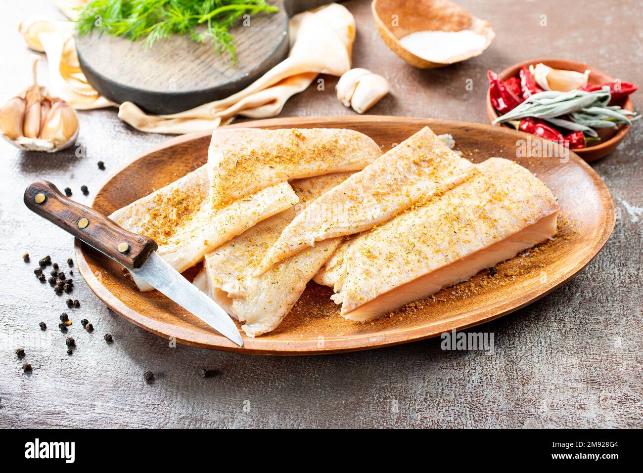 Fresh raw fish fillet with spices, pepper, salt, basil on a stone plate ...