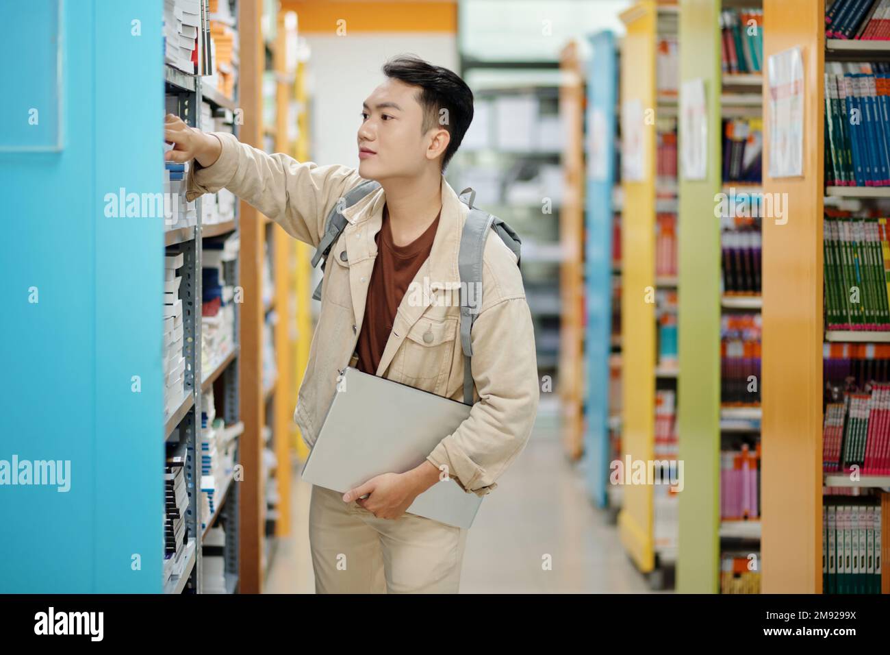 College student taking book from shelf in library Stock Photo - Alamy
