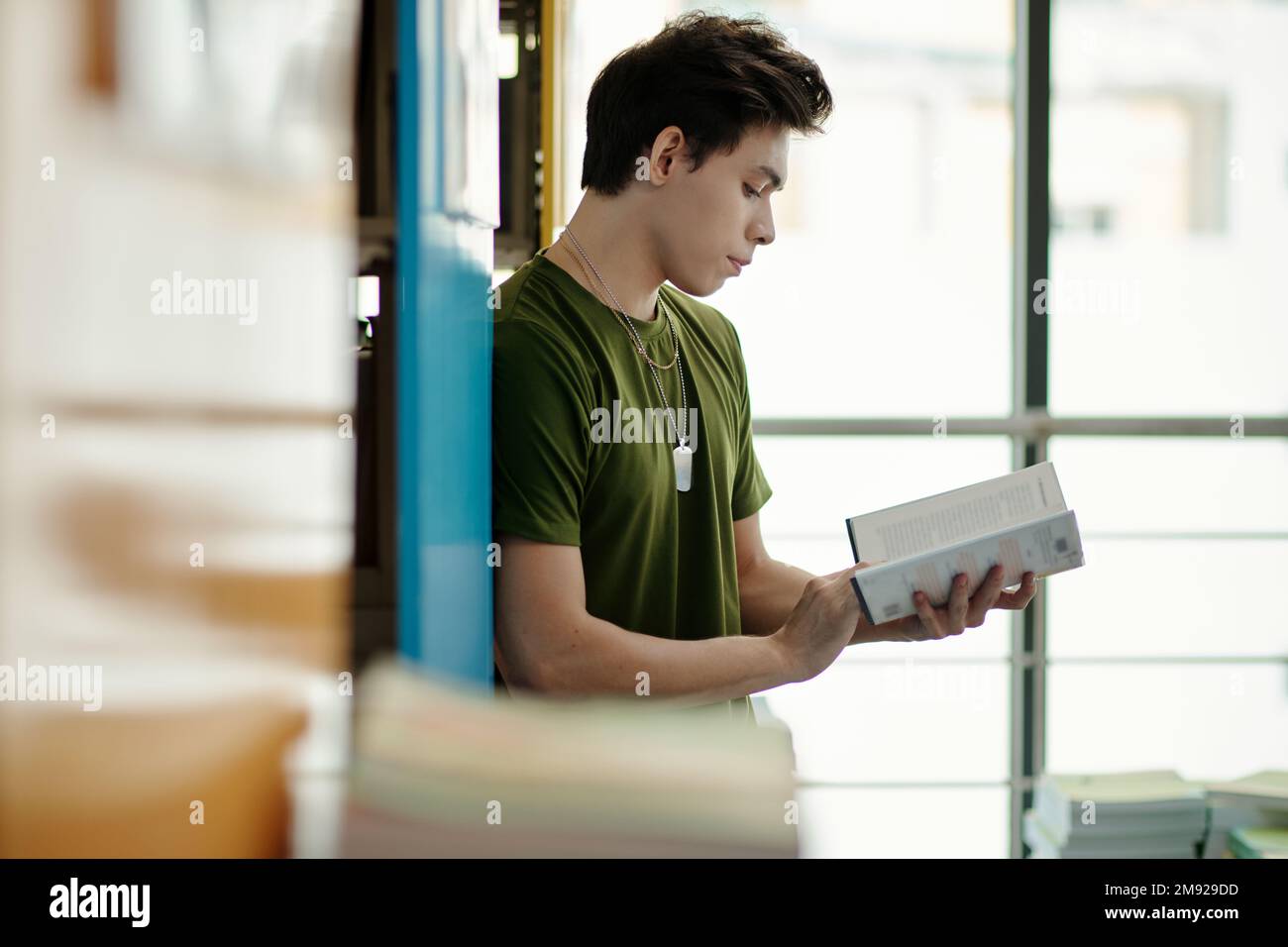 Teenage boy standing in library and reading book Stock Photo - Alamy