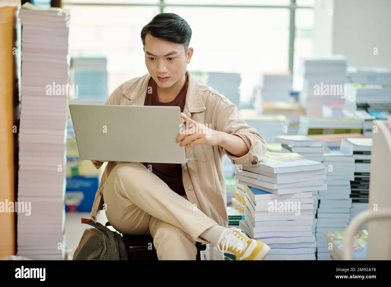 Smart college student sitting near stack of books and reading article ...